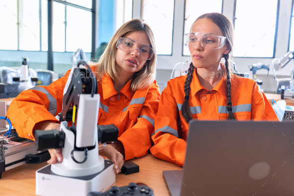 Girls engineer in robot factory fabrication room look at laptop ...