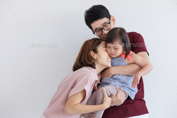 Parents kissing their daughter's cheeks together Stock Photo by thanyapatm