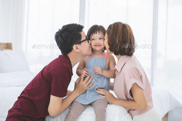 Parents kissing their daughter's cheeks together Stock Photo by thanyapatm