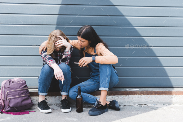upset and pretty teens sitting, talking and holding cigarettes Stock ...
