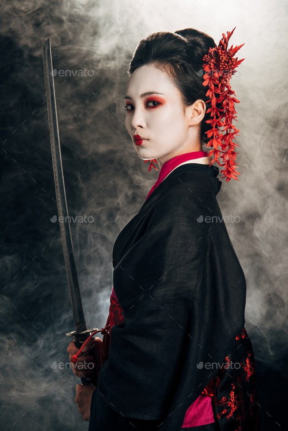 side view of beautiful geisha in black kimono holding katana in smoke ...