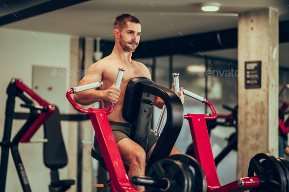 A young focused shirtless muscular sportsman is exercising on a chest ...