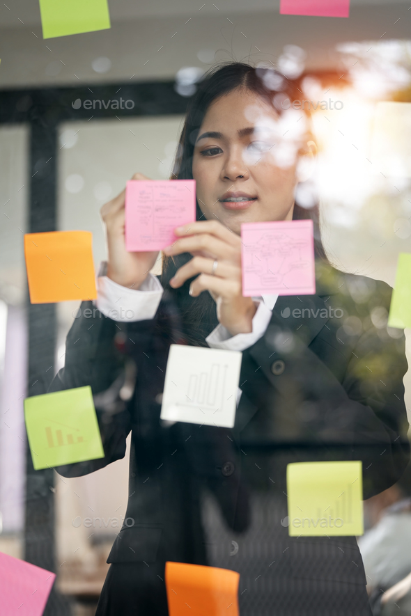 businesswoman using post it notes in glass wall to writing strategy ...