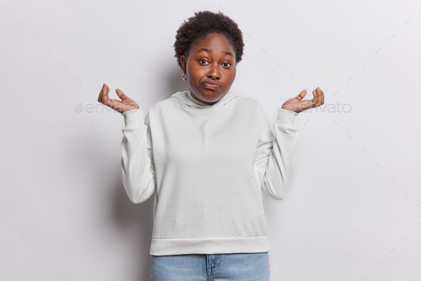 Confused Afro American woman spreads palms looks doubtfully and makes ...