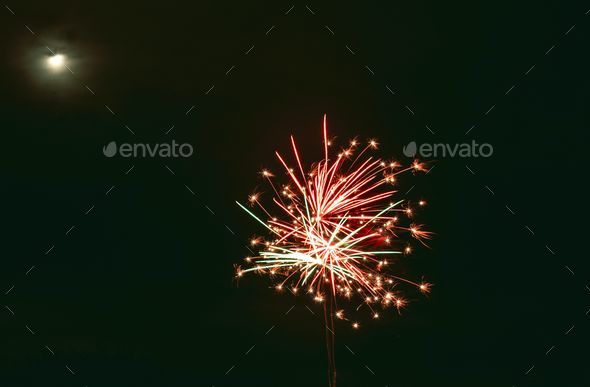fireworks light up the night sky with a half full moon behind Stock ...