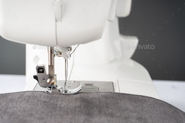 Modern sewing machine presser foot with gray fabric and thread, closeup ...