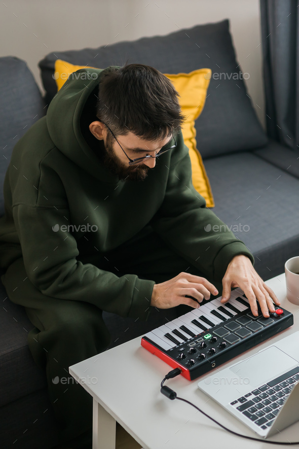 Man Recording Electronic Music Track With Portable Midi Keyboard On Laptop Computer In Home