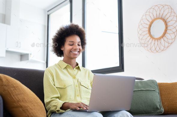 Excited cheerful young Black woman using laptop computer on sofa at ...