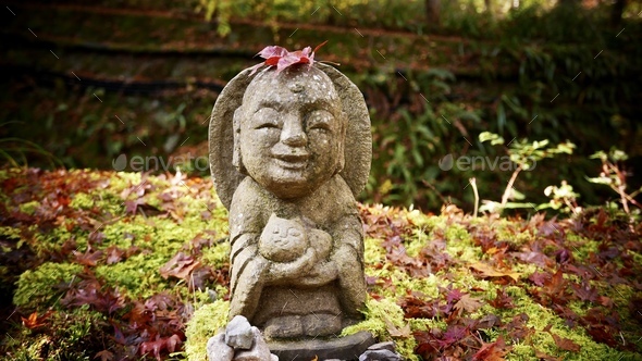 Closeup of a stone statue of a smiling Jizo Bosatsu holding a cat in ...