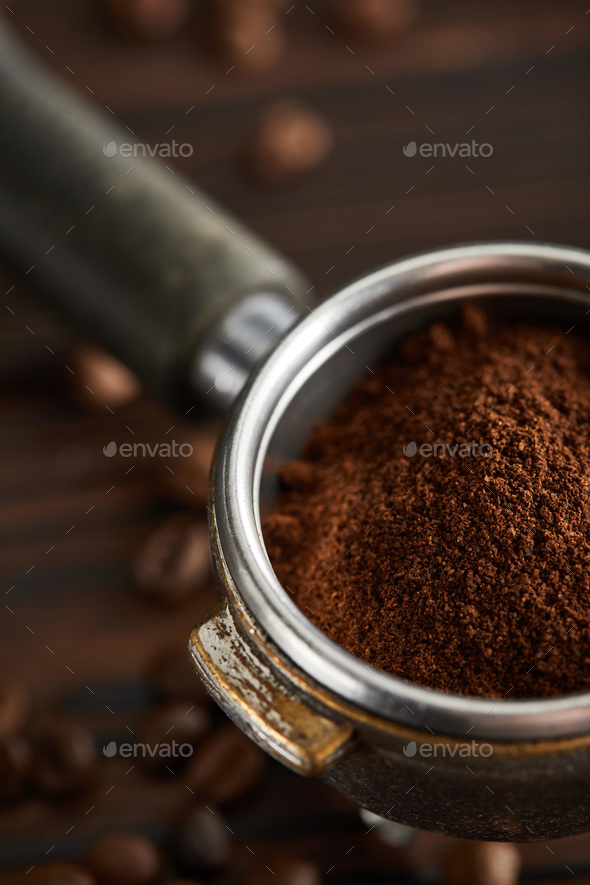 Portafilter filled with fresh ground coffee under dark surface with ...