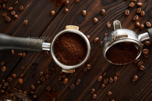 Portafilters with ground coffee on dark brown wooden surface with ...