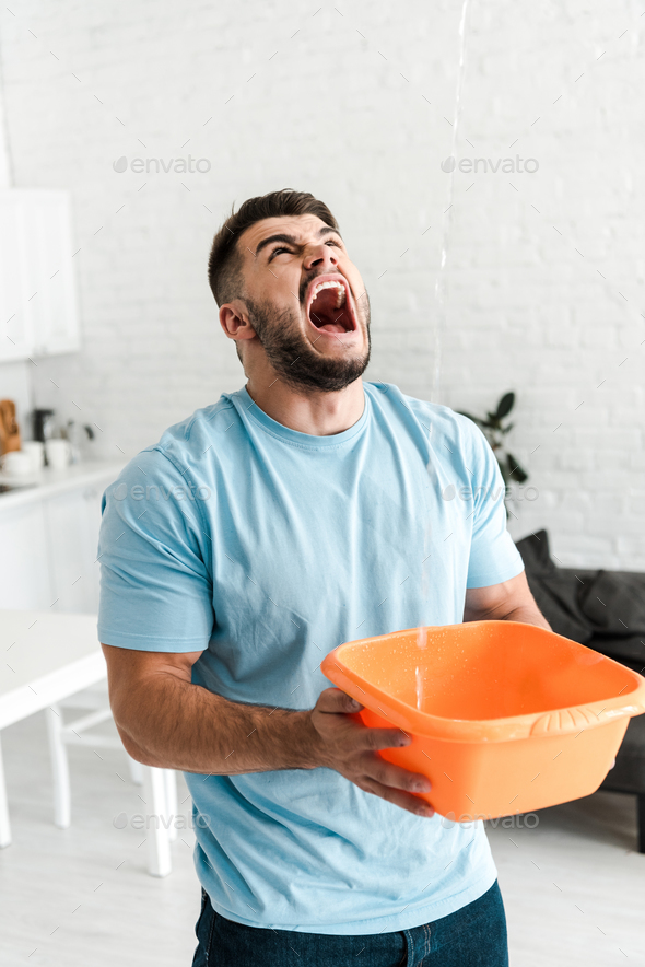 selective focus of upset man screaming while holding plastic wash bowl ...