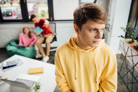 pensive boy in yellow hoodie and laughing classmates bullying him Stock ...