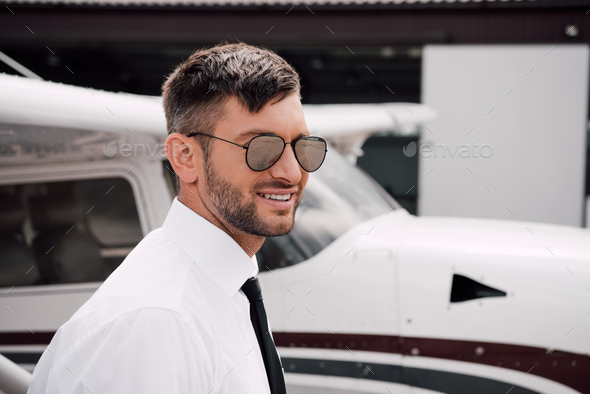 bearded pilot in formal wear and sunglasses smiling near plane Stock ...