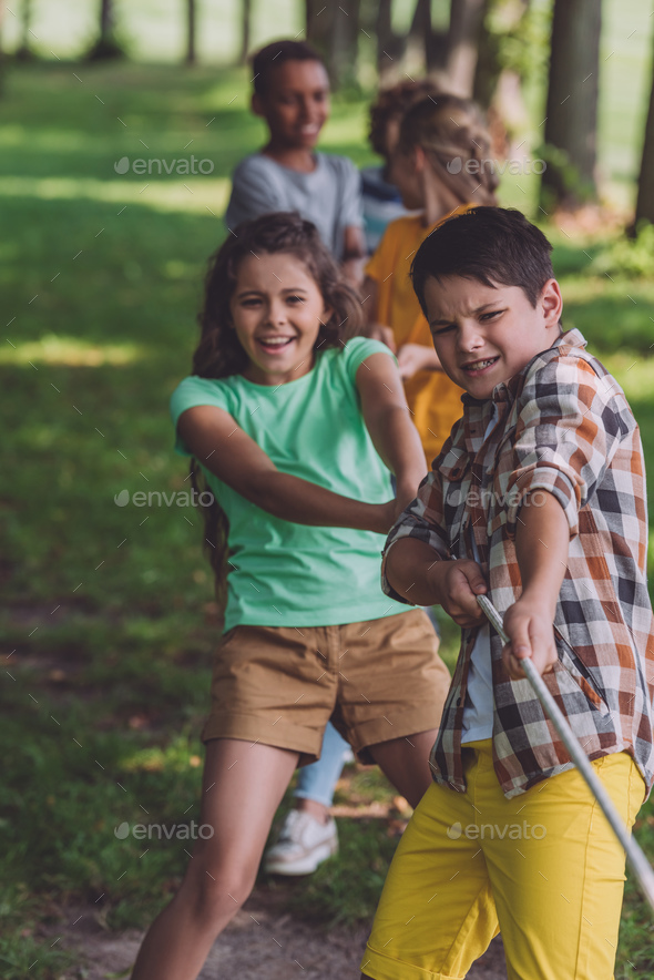 selective focus of positive multicultural kids competing in tug of war ...