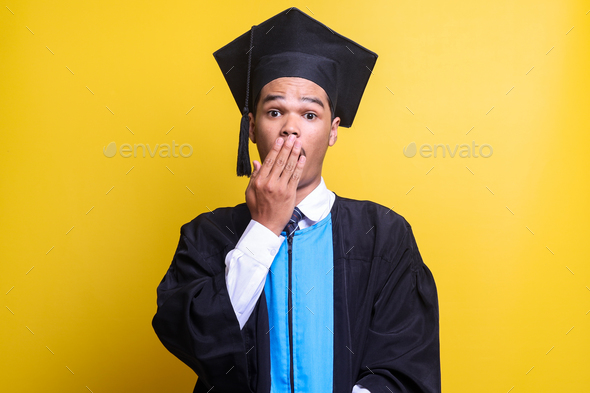 Young man in graduation cap and ceremony robe afraid and shocked ...