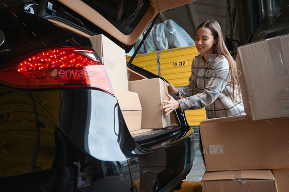 Smiling grown woman packing a box into the trunk Stock Photo by svitlanah
