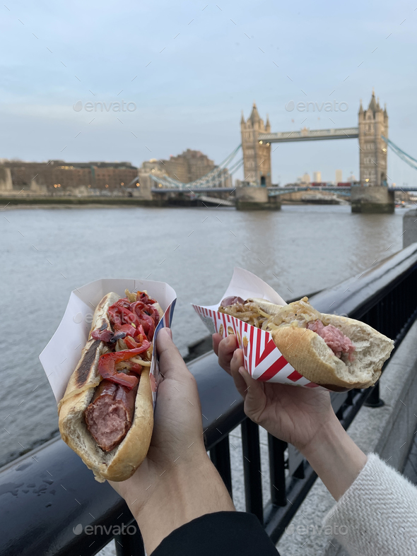 Couple hands holding hot dogs with tower bridge in background. Stock ...