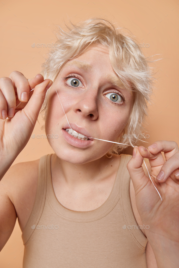 Tooth care routine concept. Blonde young woman uses teeth floss cleans ...