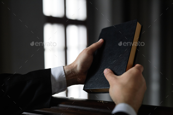 Priest holding Bible during praying Stock Photo by seventyfourimages