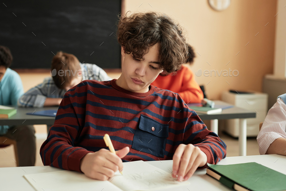 Teenage boy writing in notebook during school class Stock Photo by ...