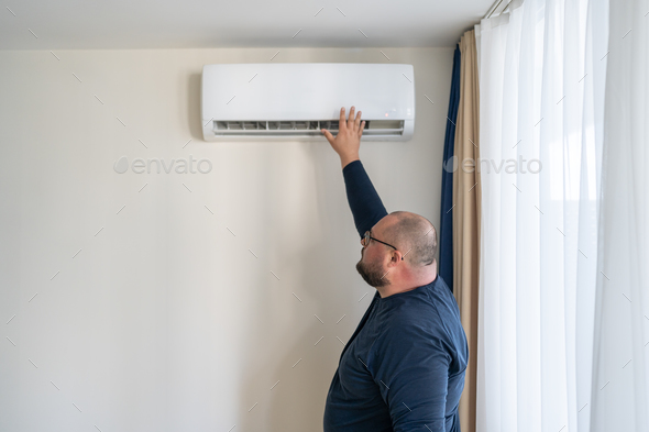 Man checking working air conditioner touching air by hand in summer hot ...