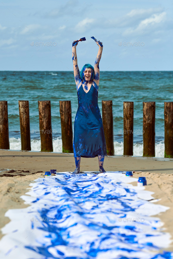 Happy woman performance artist in blue dress smeared with blue gouache ...