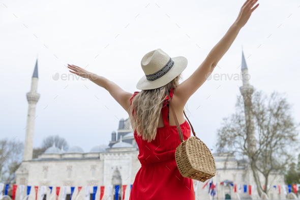 A beautiful travel blogger girl in a long red dress and a straw hat is ...
