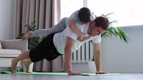 happy father doing push up exercise with son on back at gym. little boy ...