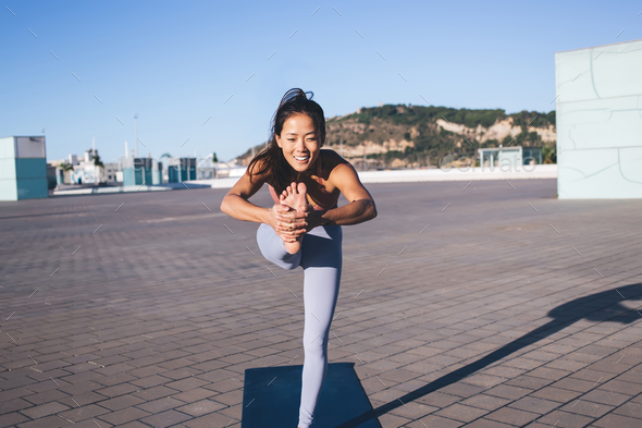 Cheerful Asian woman standing in asana on one leg recreating keeping ...
