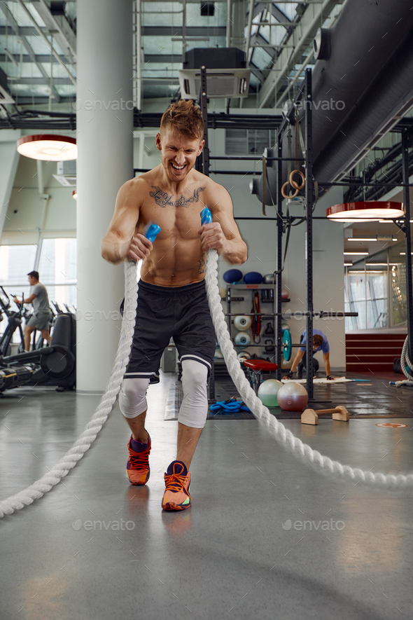 Muscular powerful aggressive man training with rope in functional ...