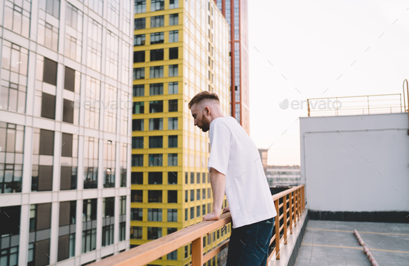 Man leaning on railing of roof near urban buildings Stock Photo by GaudiLab