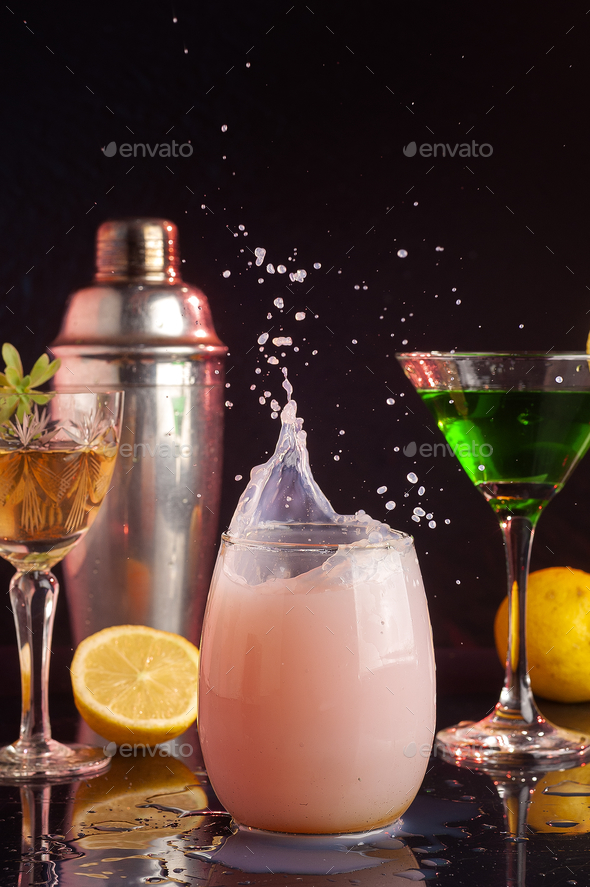 Vertical closeup of a pink cocktail with ice spilling on a bar table ...