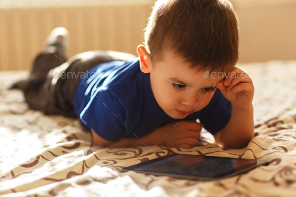 Little boy looking at tablet while lying on bed. Stock Photo by ...