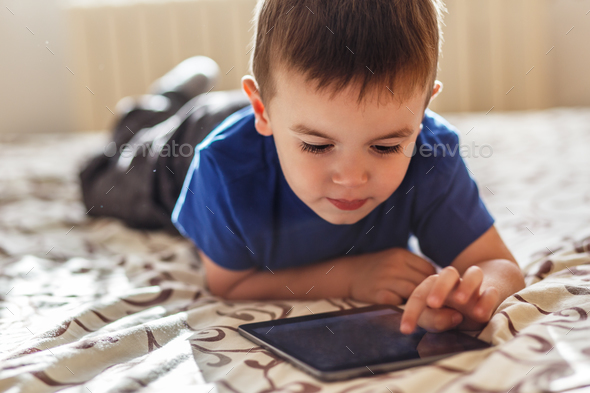 Little boy looking at tablet while lying on bed. Stock Photo by ...