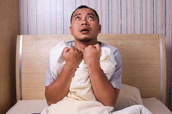 man sitting in bed stressed and scared suffering from nightmare with ...