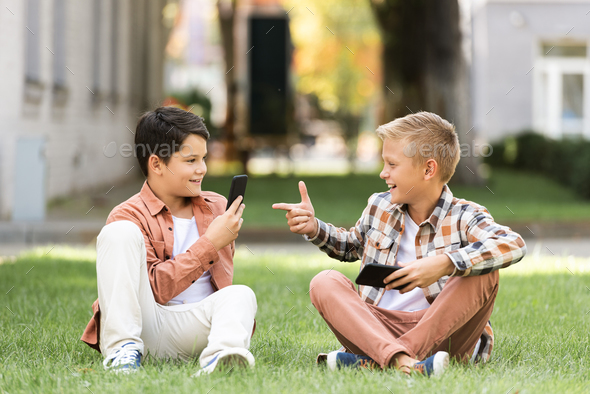 cheerful boy pointing with finger at smiling brother while sitting ...