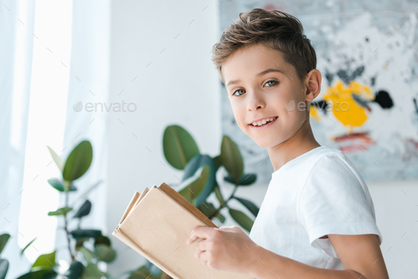 happy and cute kid holding book at home Stock Photo by LightFieldStudios