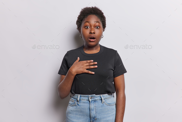 Shocked dark skinned woman feels scared looks stunned and amazed keeps ...