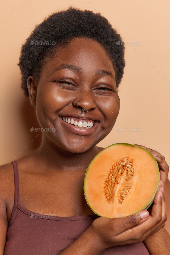 Dark skinned Afro woman with short hair holds half of melon smiles ...