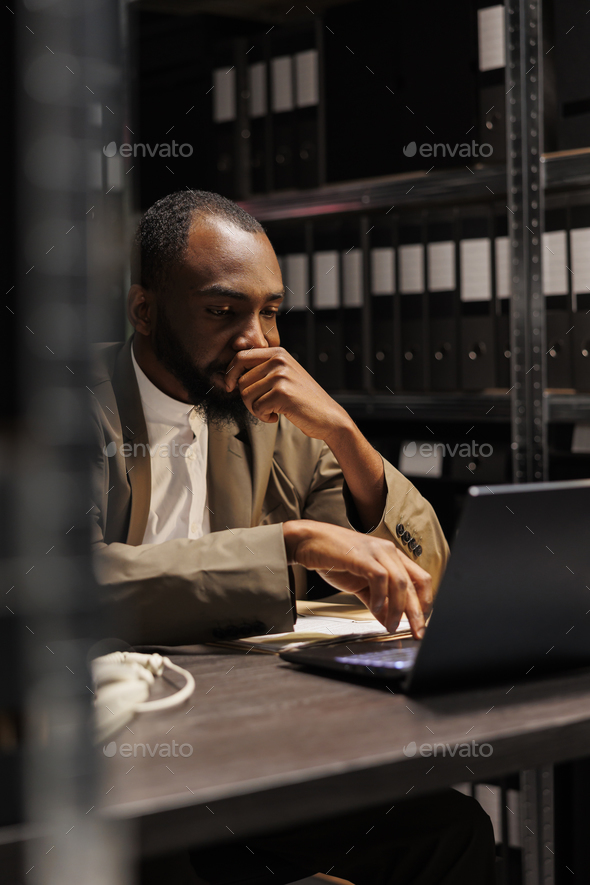 Tired cop thinking while solving case using laptop Stock Photo by DC_Studio