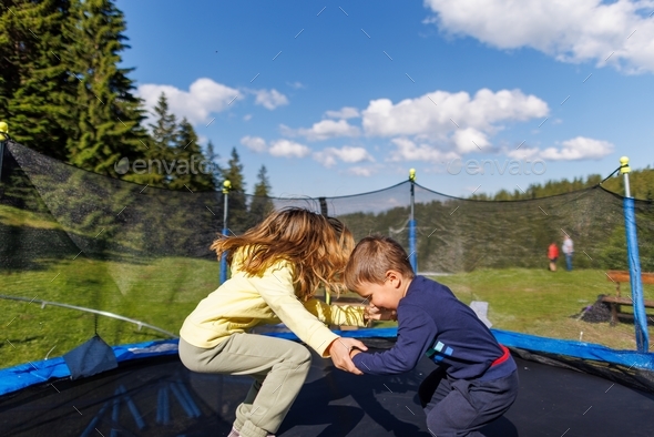 Older sister and her little brother are jumping together on a netted ...