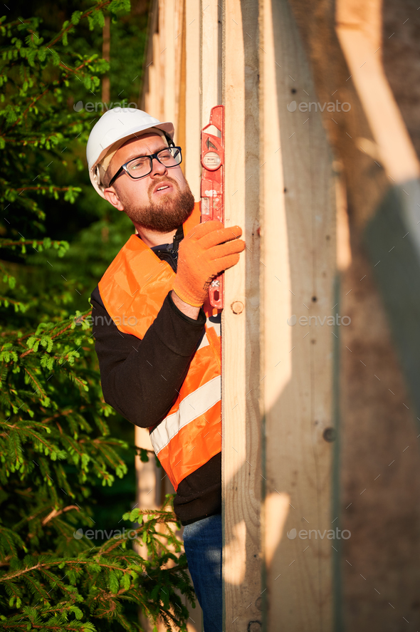 Carpenter using spirit level while constructing wooden frame house ...
