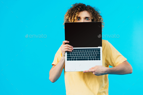 scared curly student hiding behind laptop with blank screen isolated on ...