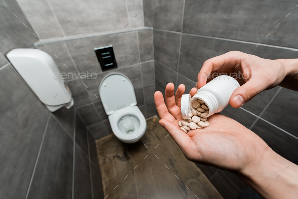 cropped view of man holding pills near ceramic clean toilet bowl in ...