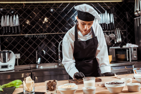 attractive chocolatier in chef hat touching caramelized nuts in ...