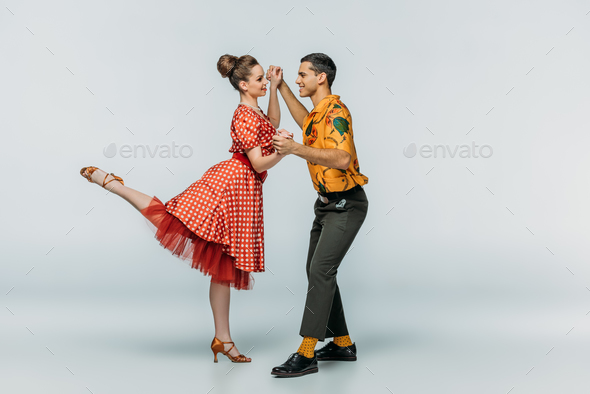 cheerful dancers holding hands while dancing boogie-woogie on grey ...