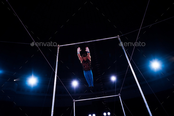 athletic gymnast jumping while performing on horizontal bars in arena ...