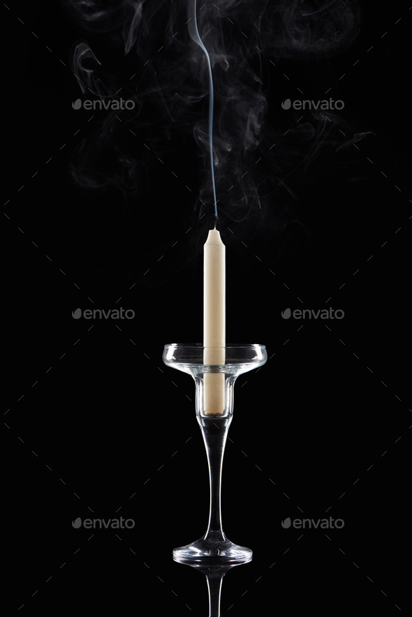 extinct white candle in glass candlestick with smoke on black ...