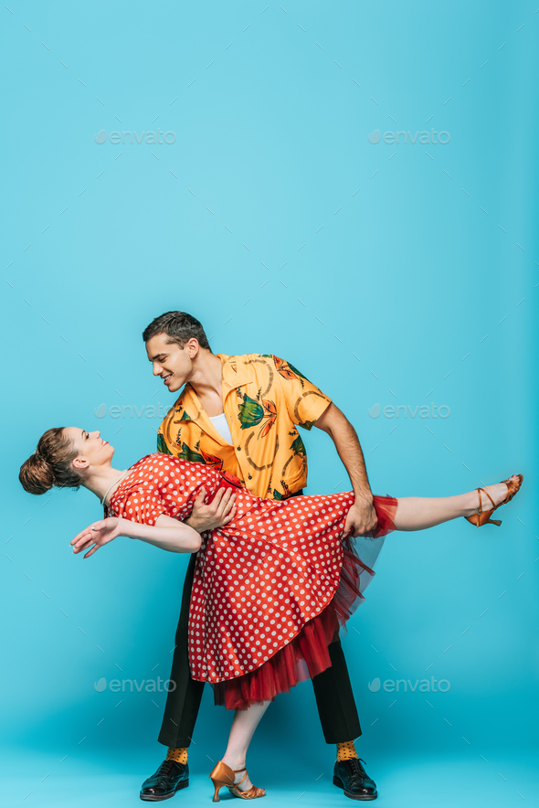 handsome dancer supporting partner while dancing boogie-woogie on blue ...